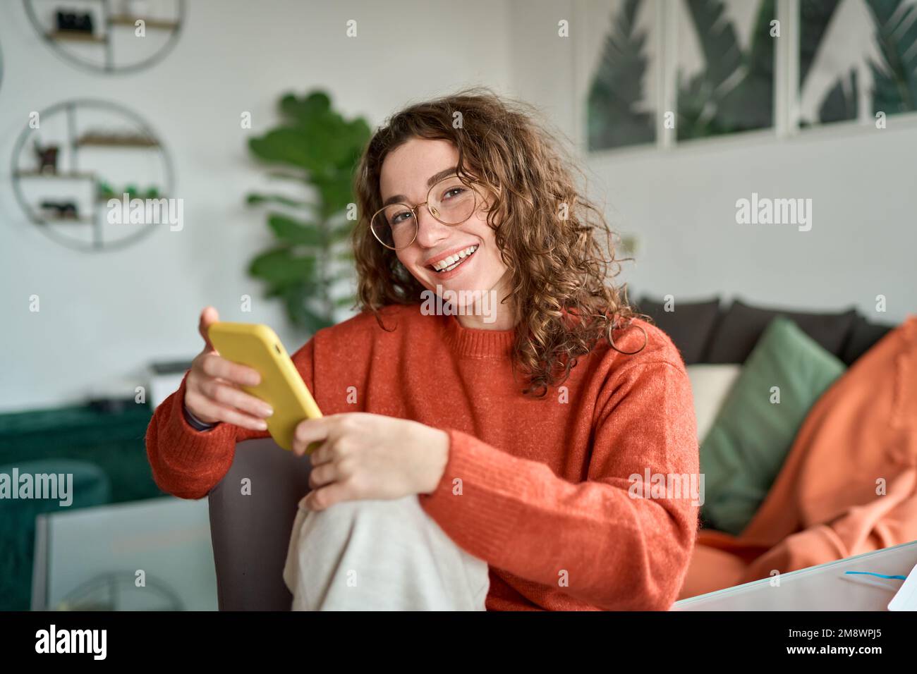 Smiling pretty young woman sitting at home using mobile cell phone ...
