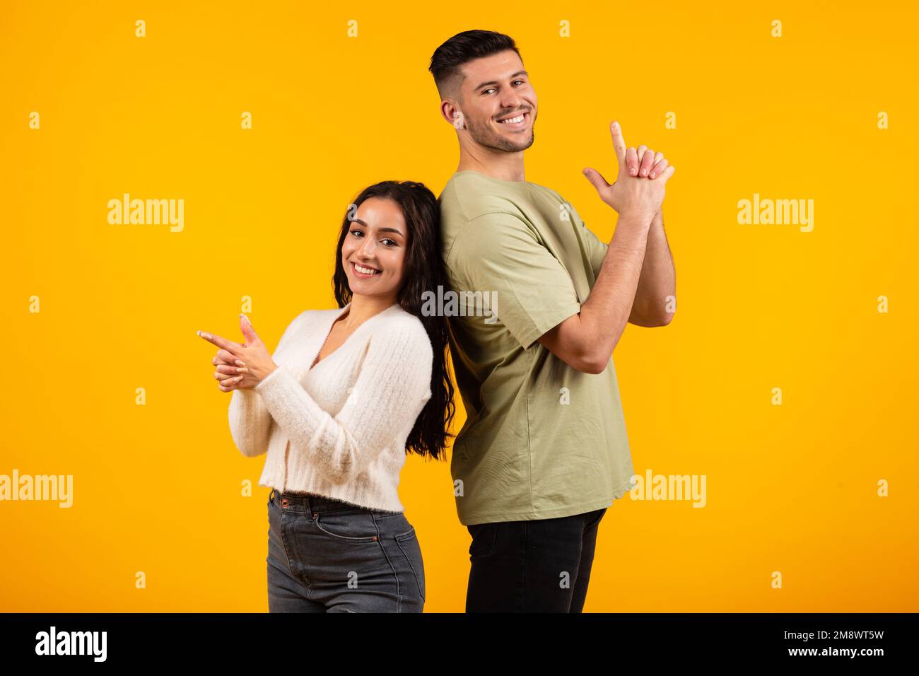 Happy millennial arabic husband and wife hold imaginary pistols, make sign with hands, have fun ...