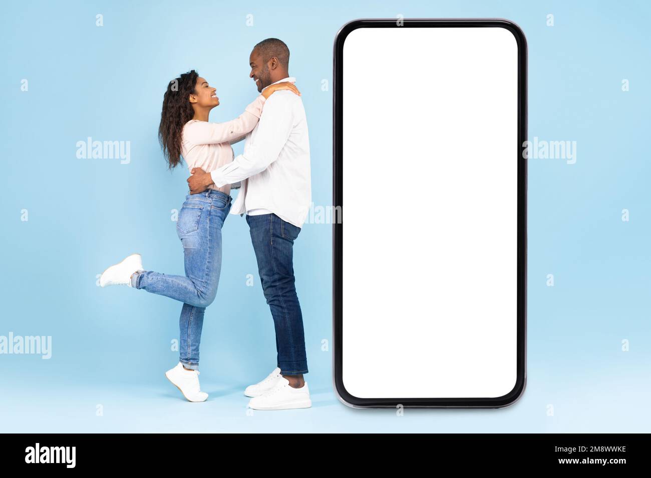 Loving black couple embracing and standing near large mobile phone with ...