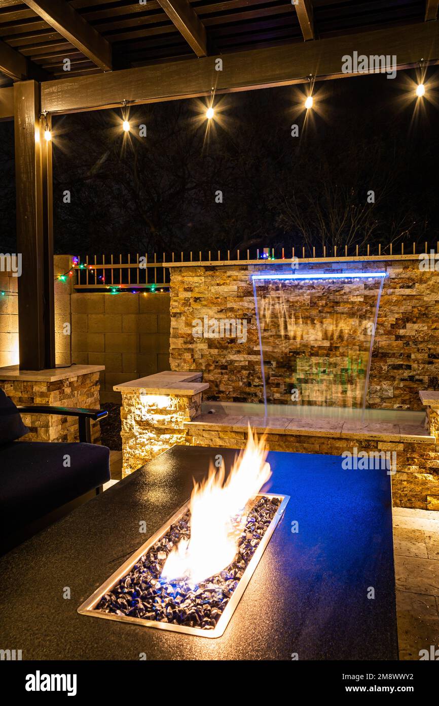 A resort style backyard at night with a waterfall, pergola, and a ...