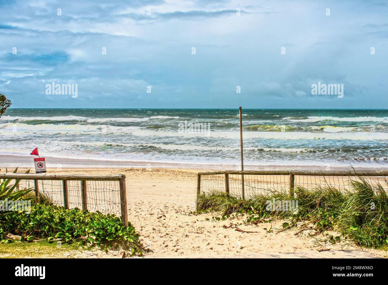 Path down to beach with wire fence and vegetation to each side, stormy ...