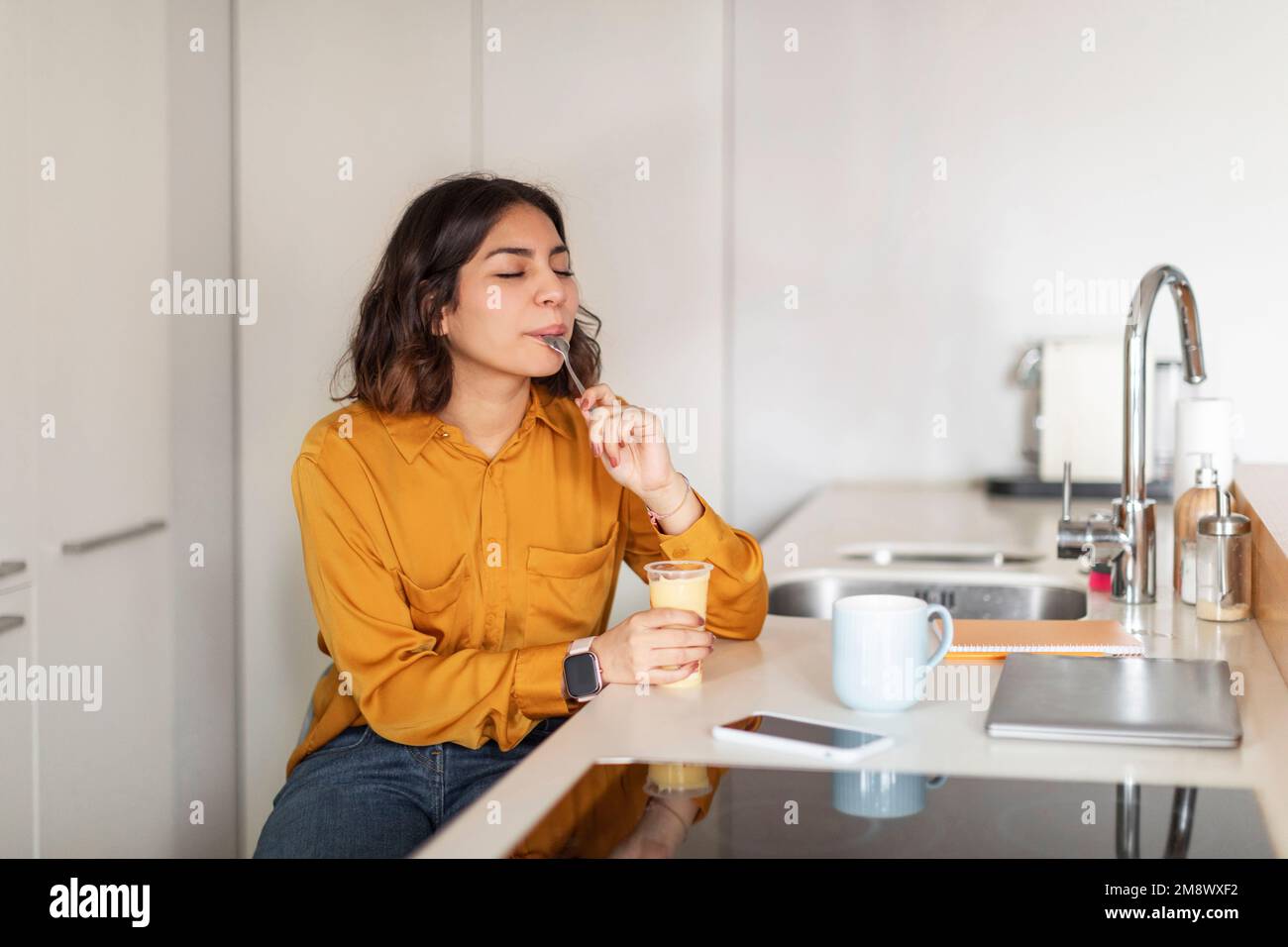 Young Woman Sitting At Kitchen Counter And Eating Pudding From Plastic ...