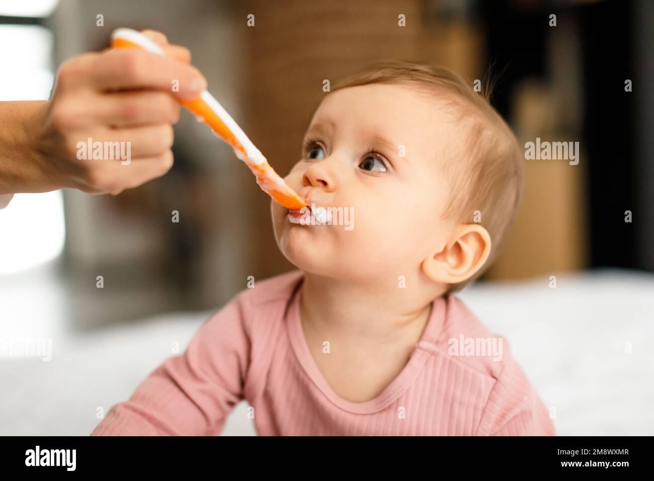Baby feeding. Cute little infant girl eating from spoon, caring mother ...
