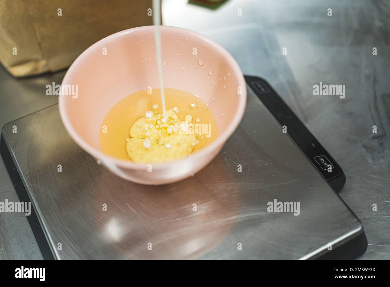 Baker pouring milk into oil in a bowl to prepare cupcake batter ...