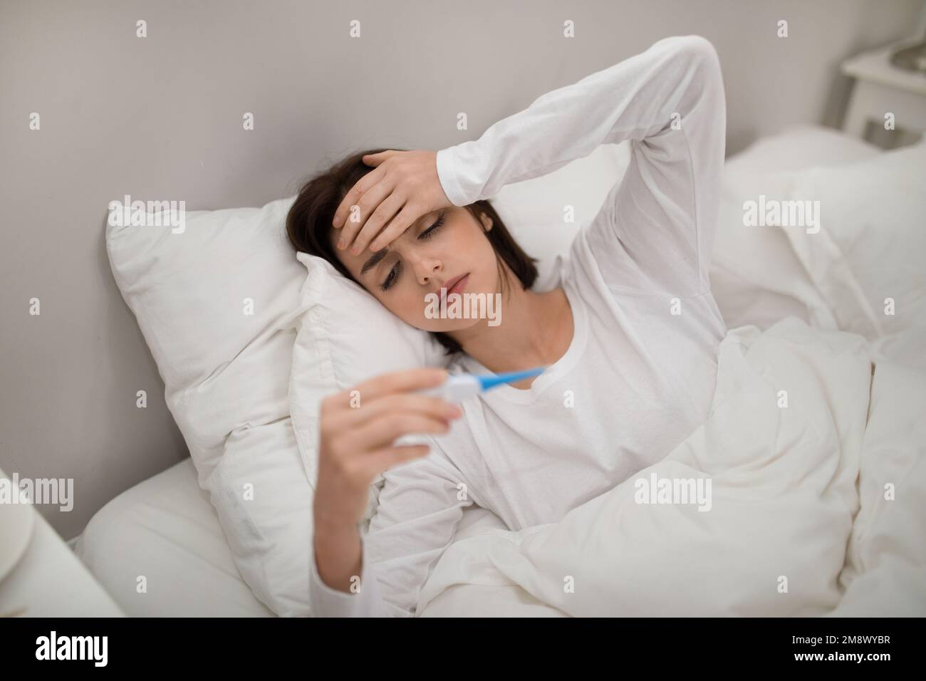 Sick woman with fever checking her temperature in bed Stock Photo - Alamy