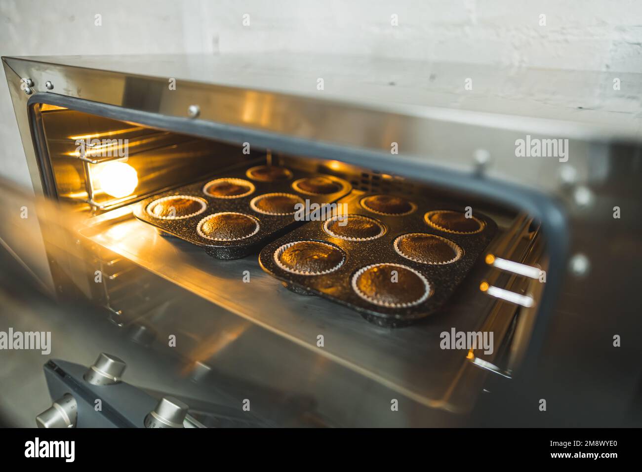 Tray of chocolate cupcakes baking in open oven with light on ...