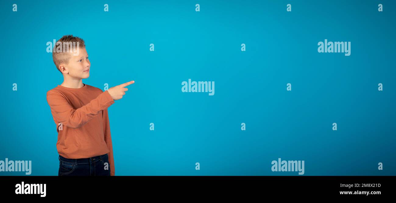 Cute smiling preteen boy pointing aside at copy space on blue ...