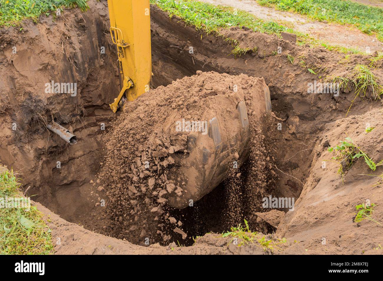 A bucket of excavator with a pile of earth digs a hole on the ...