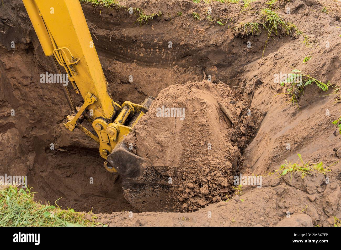 A bucket of excavator with a pile of earth digs a hole on the ...