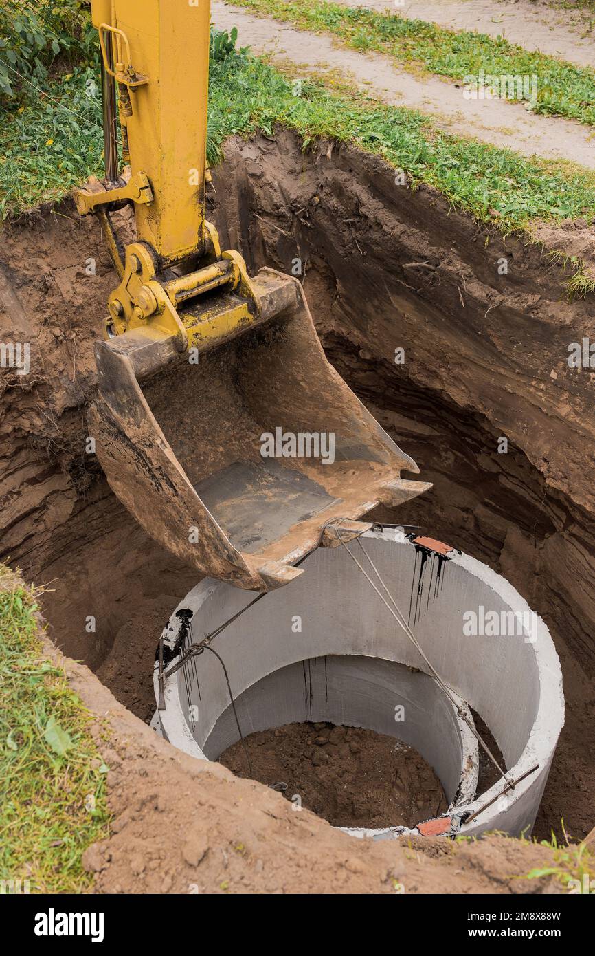 Excavator with a bucket, lowering into the pit on steel cables concrete ...