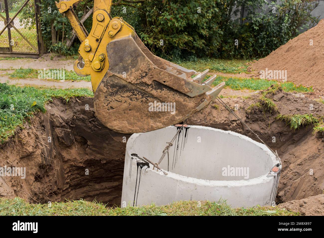 Excavator with a bucket, lowering into the pit on steel cables concrete ...