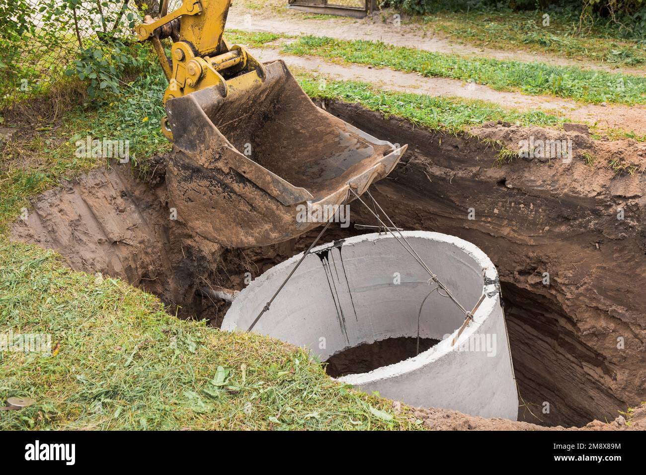 Excavator with a bucket, lowering into the pit on steel cables concrete ...