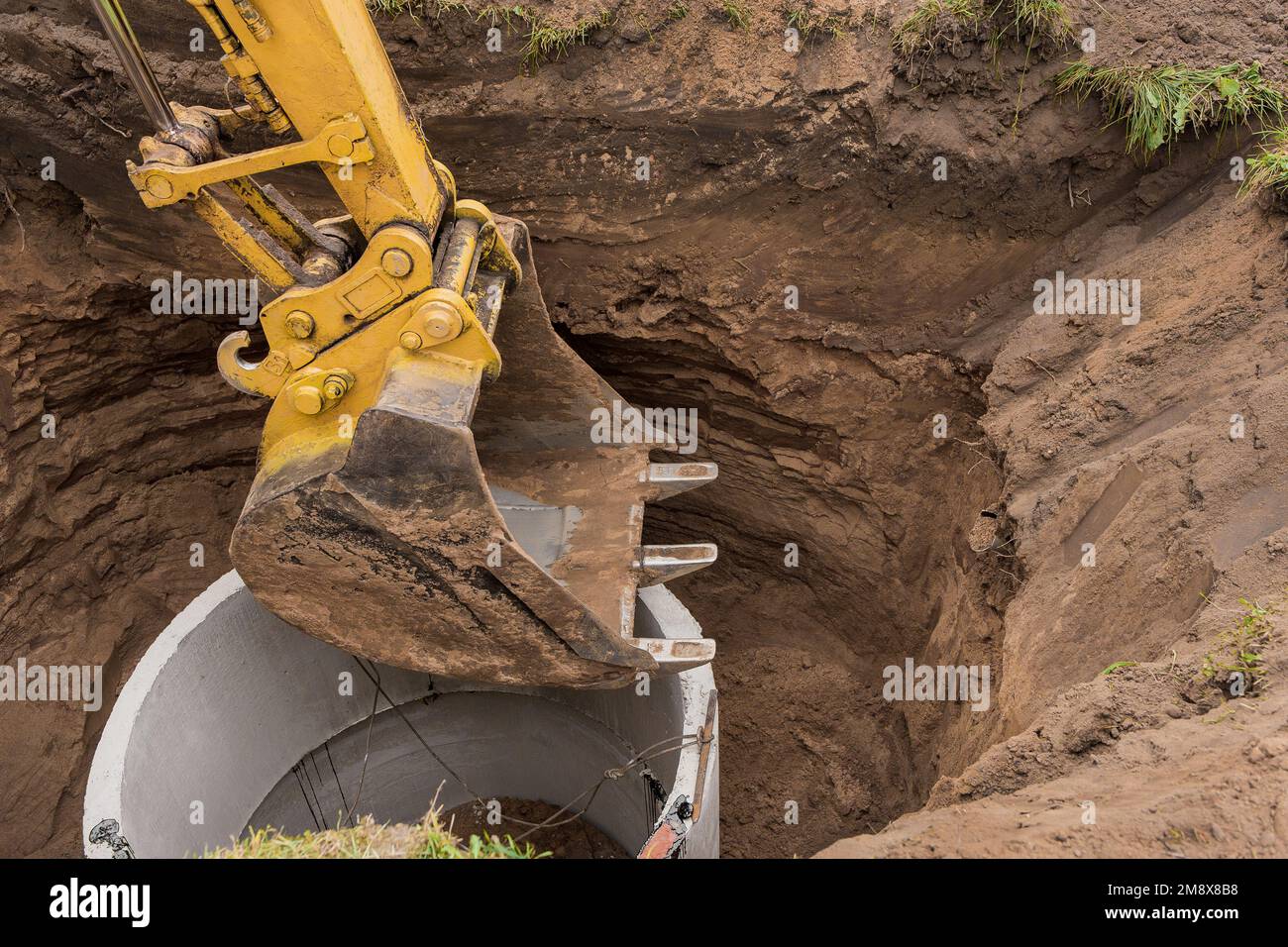 Excavator with a bucket, lowering into the pit on steel cables concrete ...