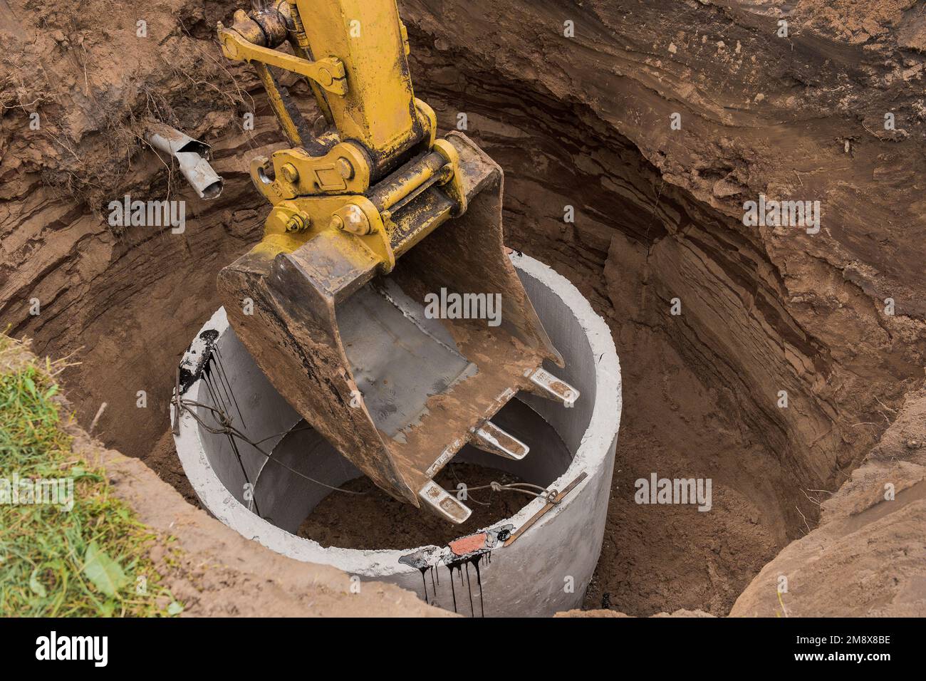 Excavator with a bucket, lowering into the pit on steel cables concrete ...