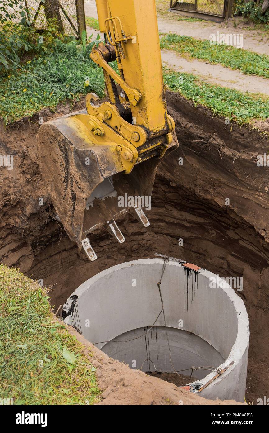 Excavator with a bucket, lowering into the pit on steel cables concrete ...