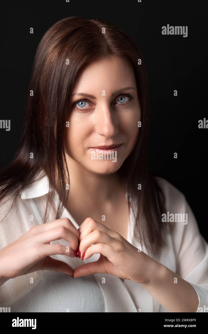 Portrait of woman showing heart shapes sign with both hands, looking at ...