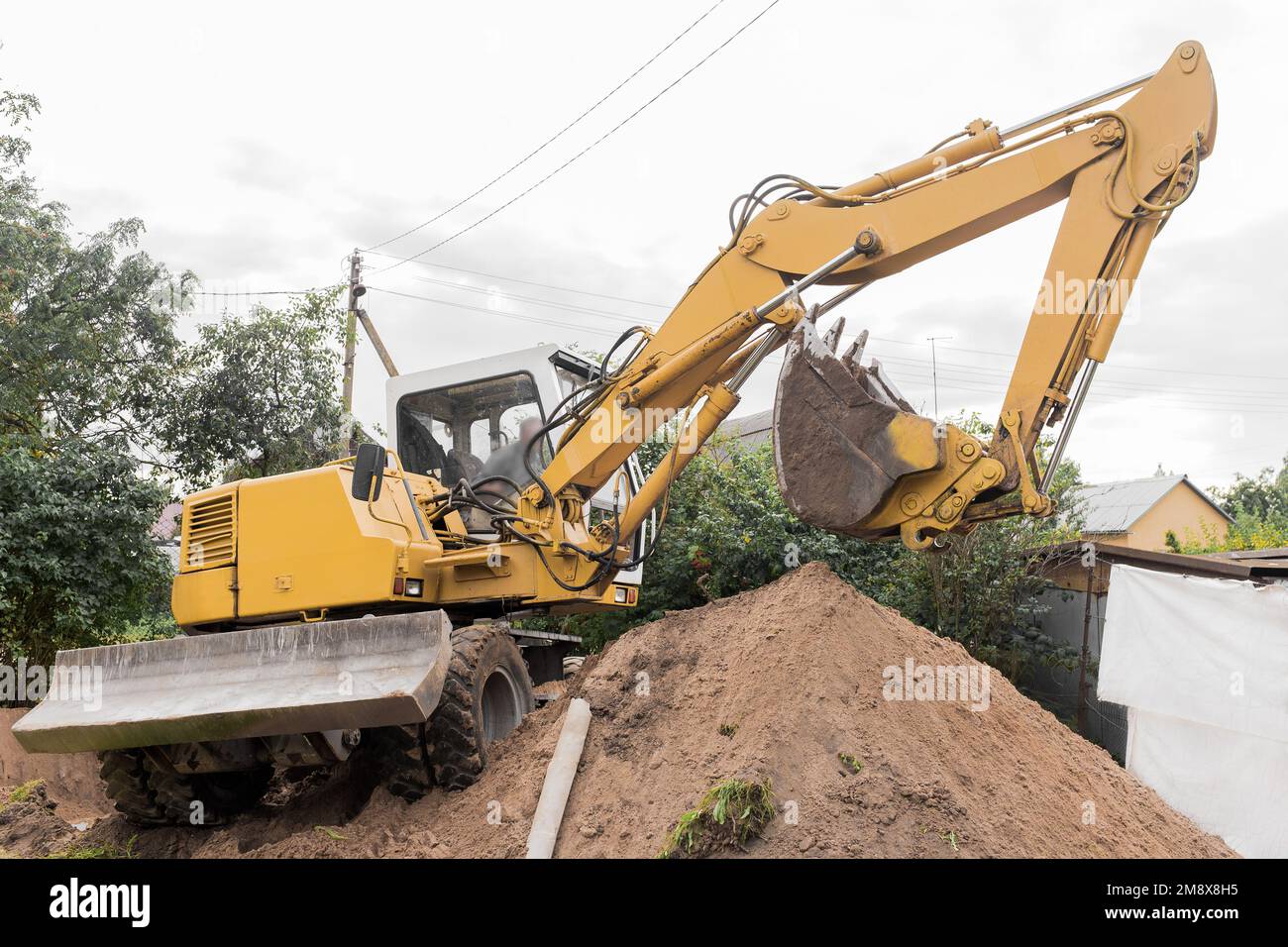 A hydraulic piston and a bucket excavator dig the ground next to a pile ...