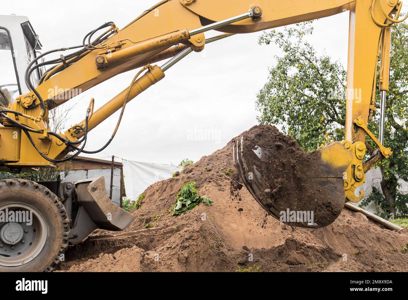 A hydraulic piston and a bucket excavator dig the ground next to a pile ...