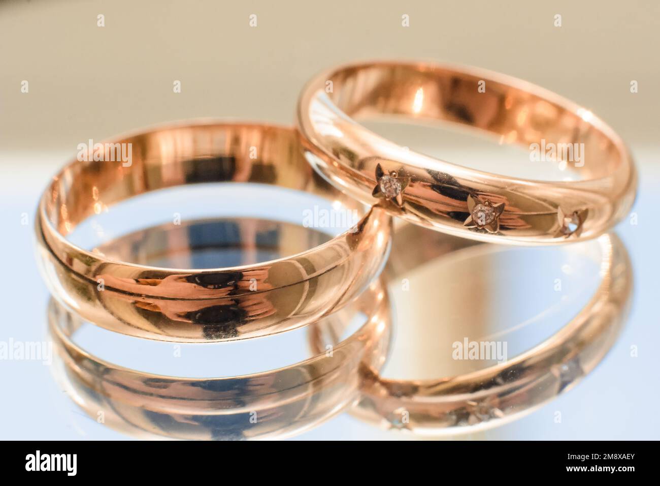 two gold wedding rings with diamonds on the surface with reflection ...