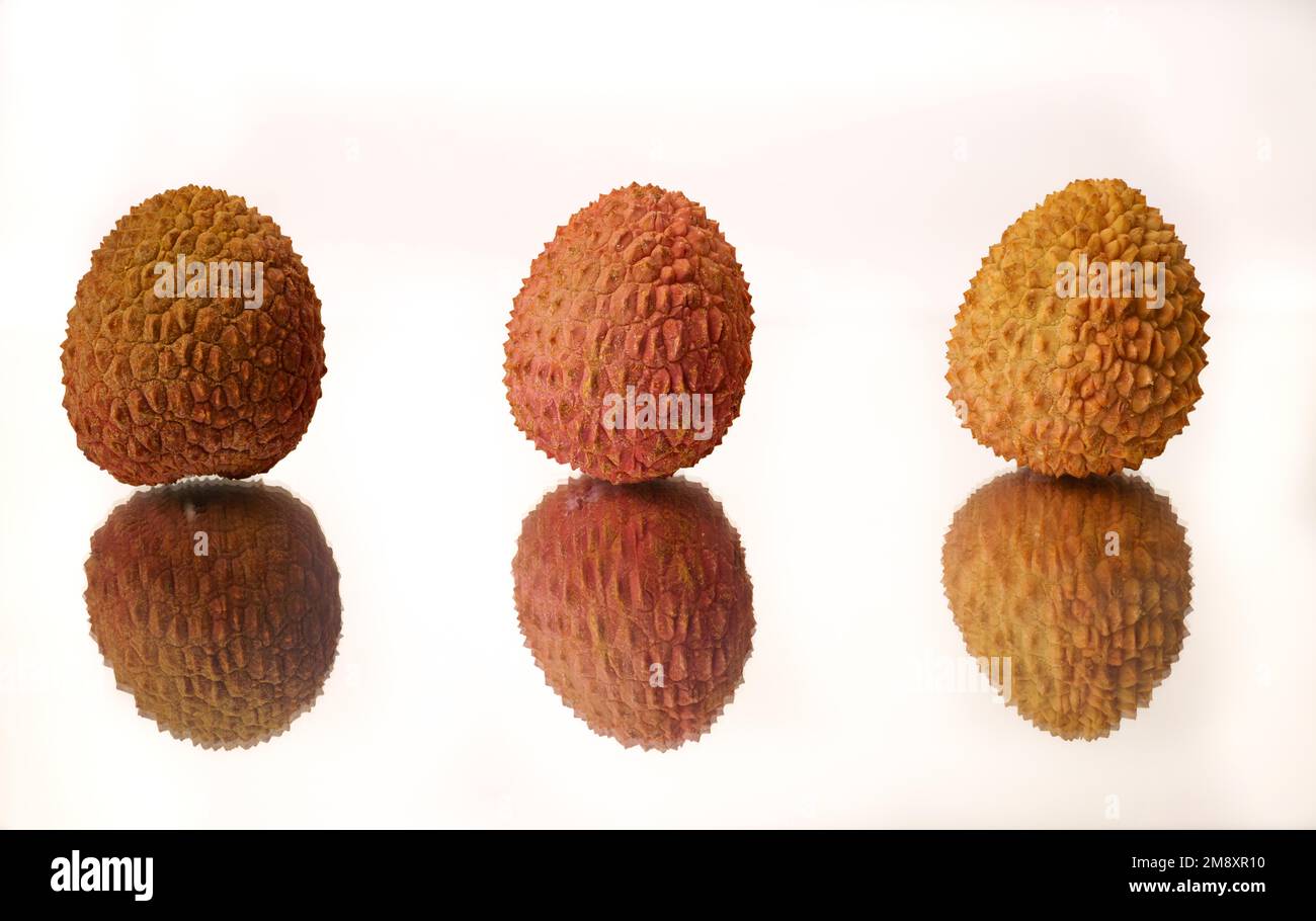 Close-up of three fresh lychees reflected in a mirror on a white ...