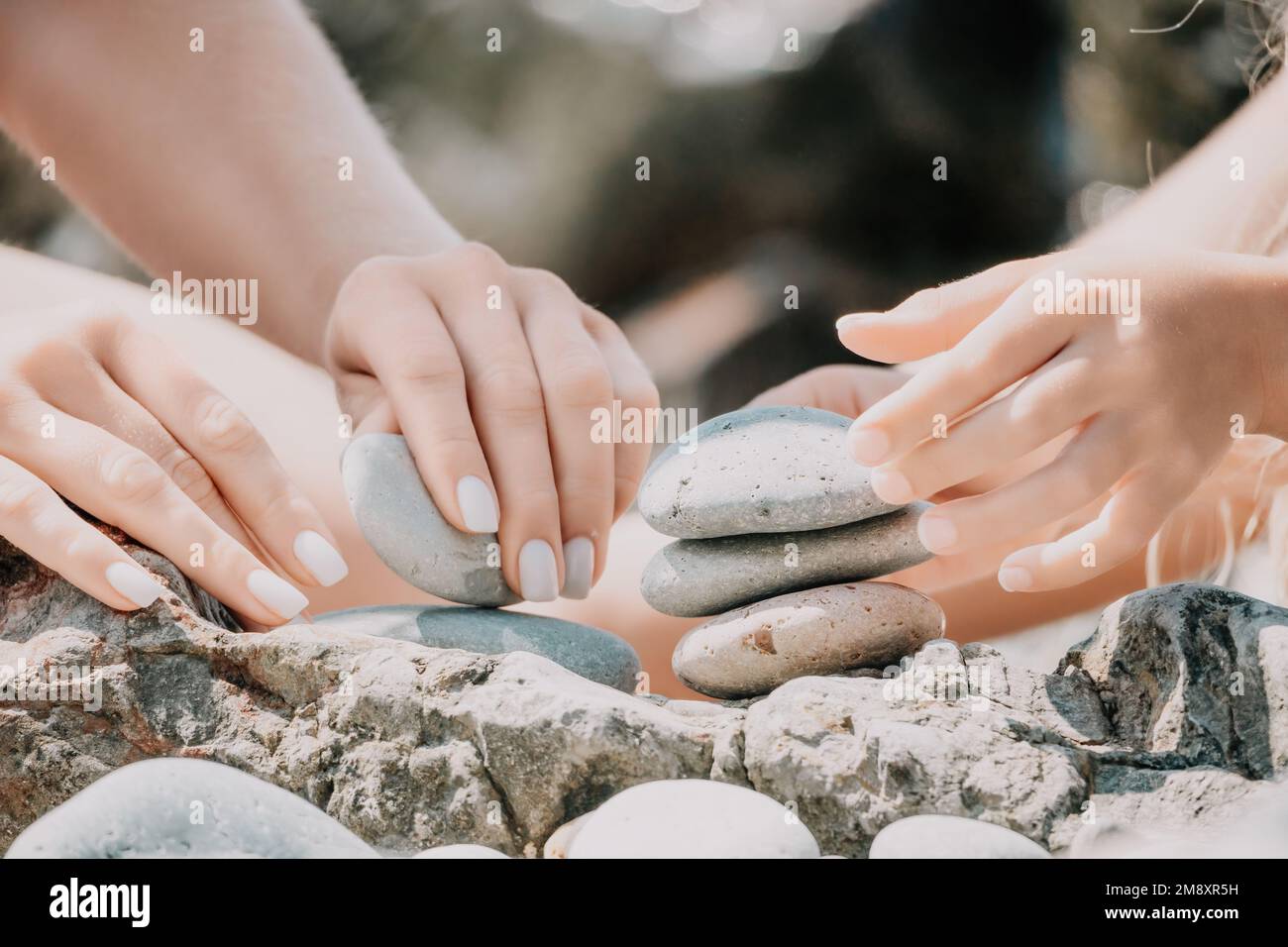 Woman with daughter bilds stones pyramid on seashore on a sunny day on ...