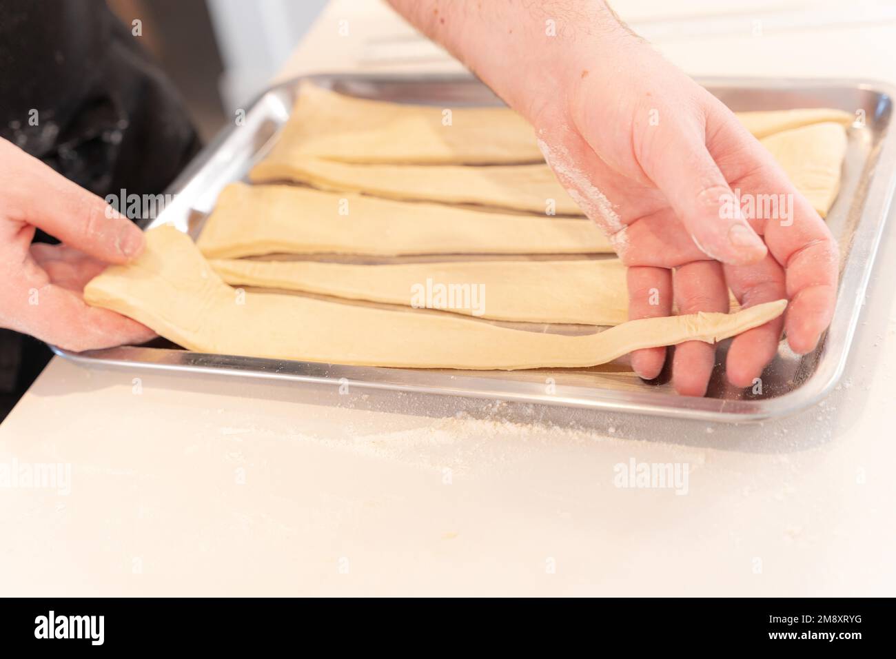 Detail of the hands of a man baking croissants making triangular cuts ...