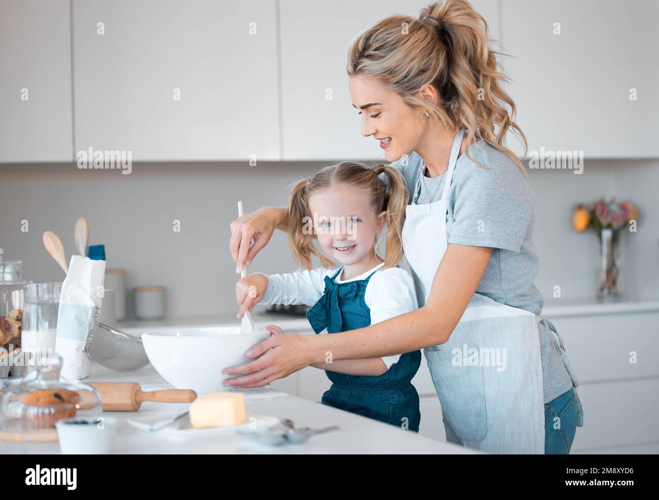 Portrait of a little girl baking with her mother. Happy mother helping her daughter bake. Parent ...
