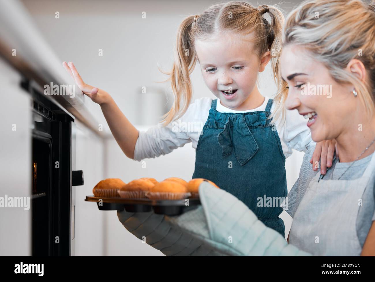 Happy mother and daughter looking at muffins. Young woman removing a ...