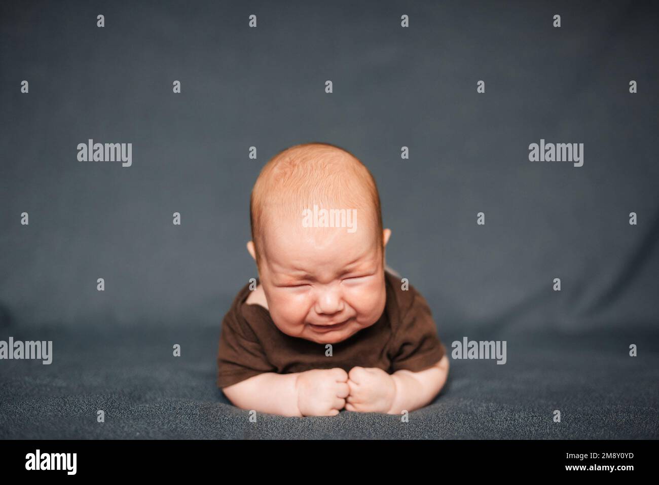 Newborn baby boy crying. The Caucasian child is lying on a grey blanket ...