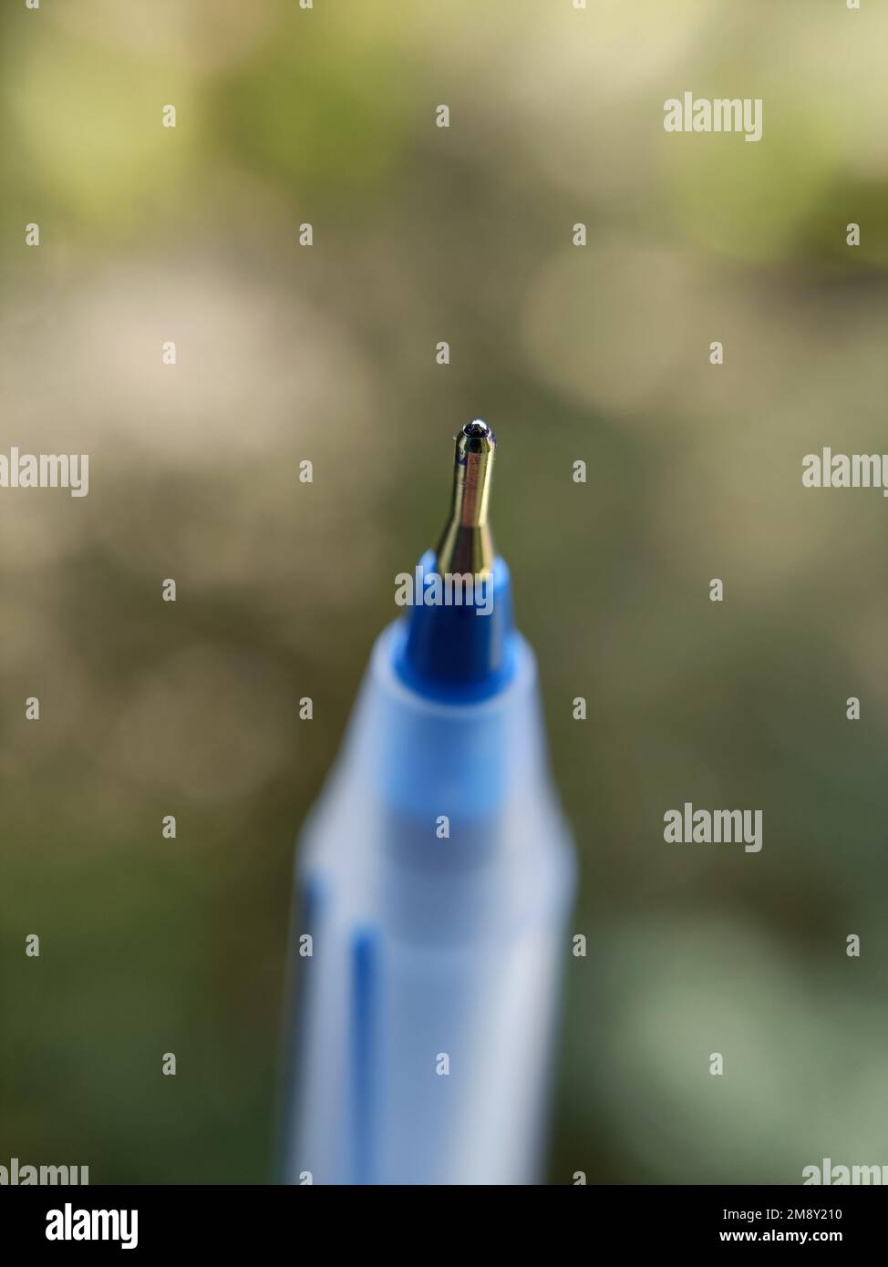 A selective focus of a blue pen's tip on a blurry green background ...