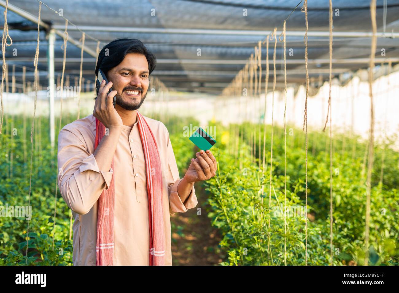 young farmer at greenhouse talking on mobile phone call by holding ...