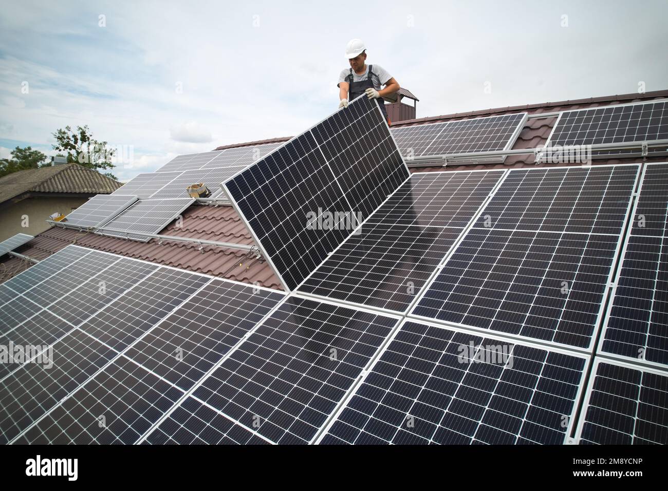 Man technician mounting photovoltaic solar moduls on roof of house. Mounter in helmet installing ...