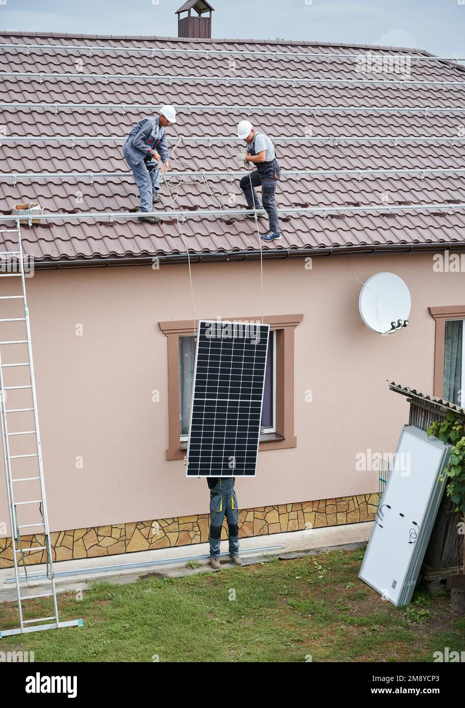Men technicians lifting up photovoltaic solar modul on roof of house ...