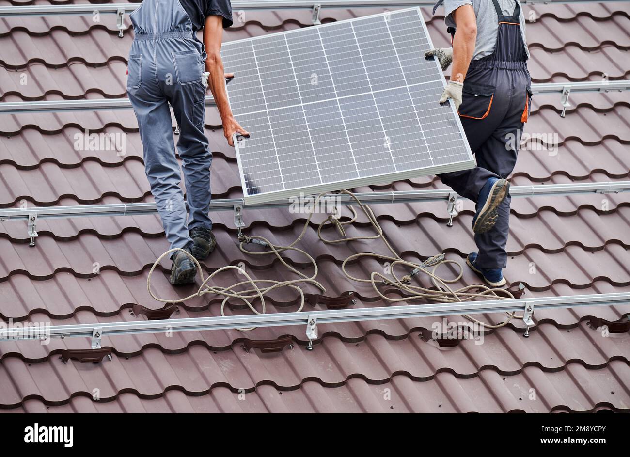 Men installers carrying photovoltaic solar moduls on roof of house ...