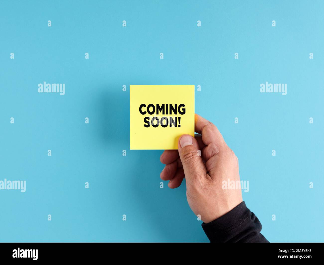 Male hand holds a yellow sticky note paper with the message coming soon ...