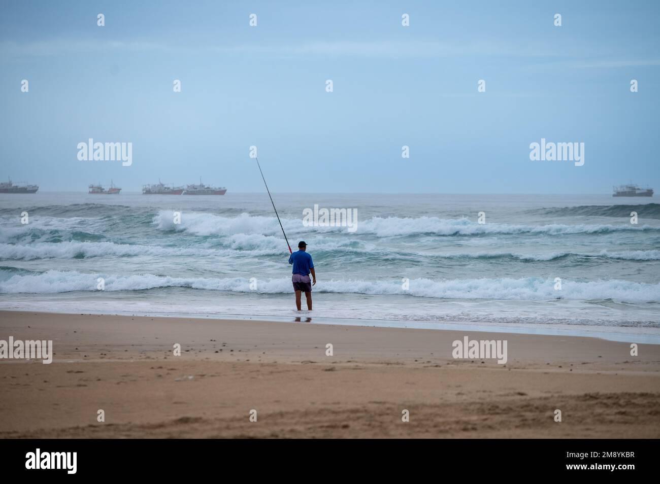Man seen fishing with trawlers in distance Stock Photo - Alamy