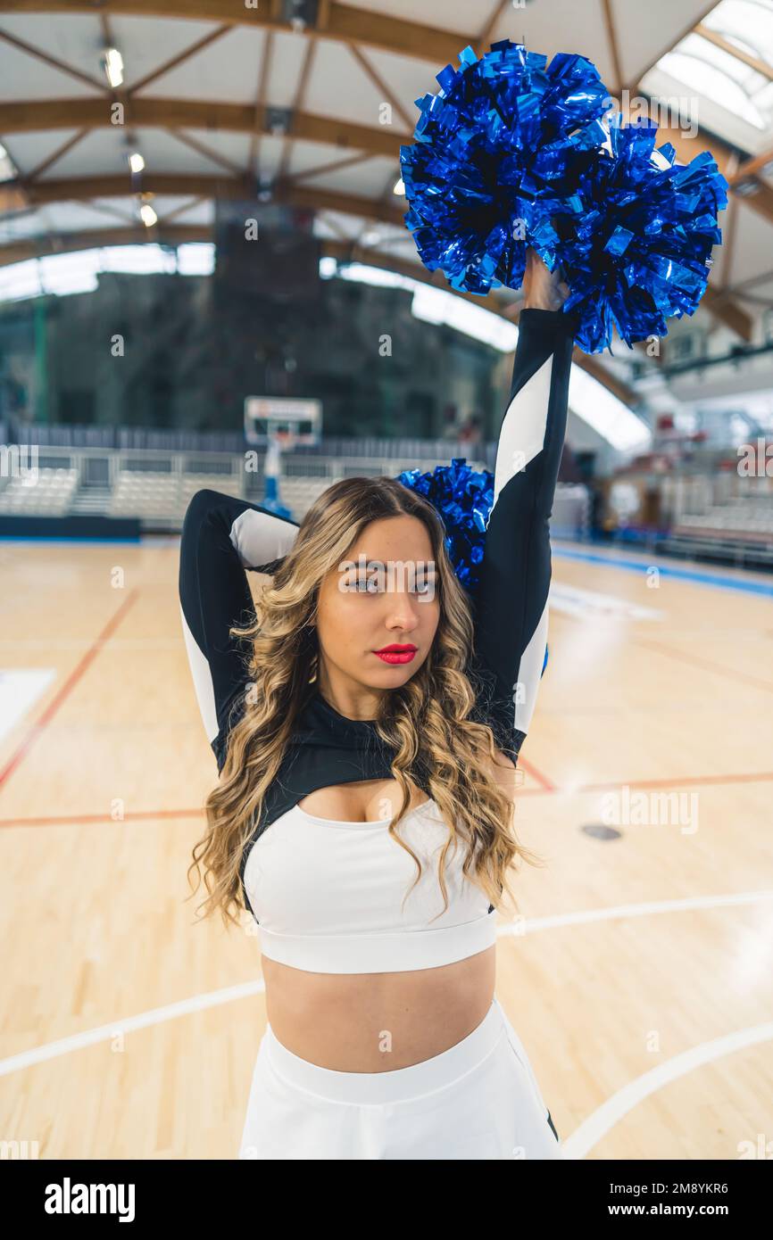 Medium shot. A blond cheerleader in an uniform, with one arm behind her ...