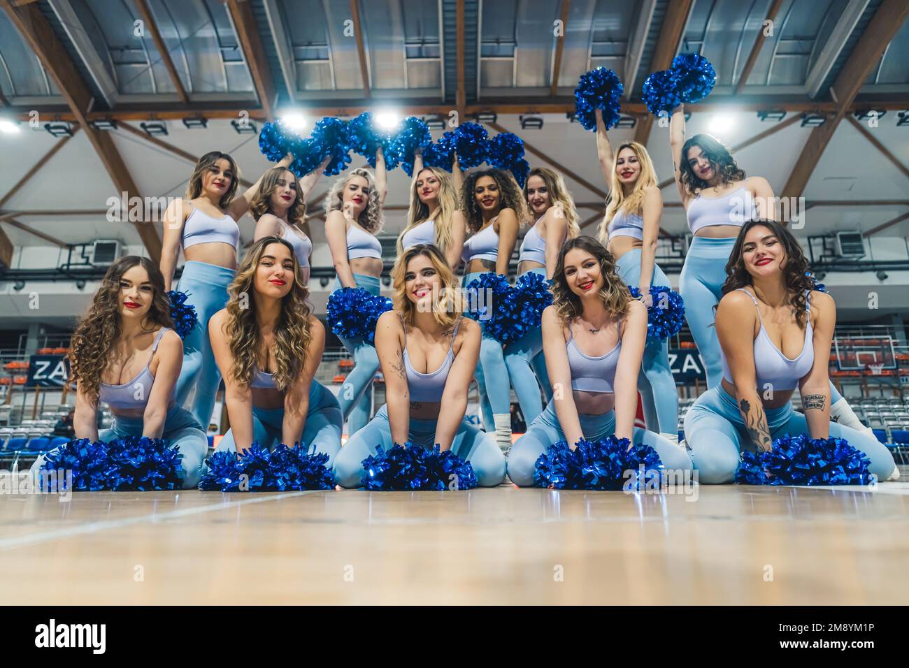Cheerleaders posing for a picture in two rows with blue pom-poms. Full ...