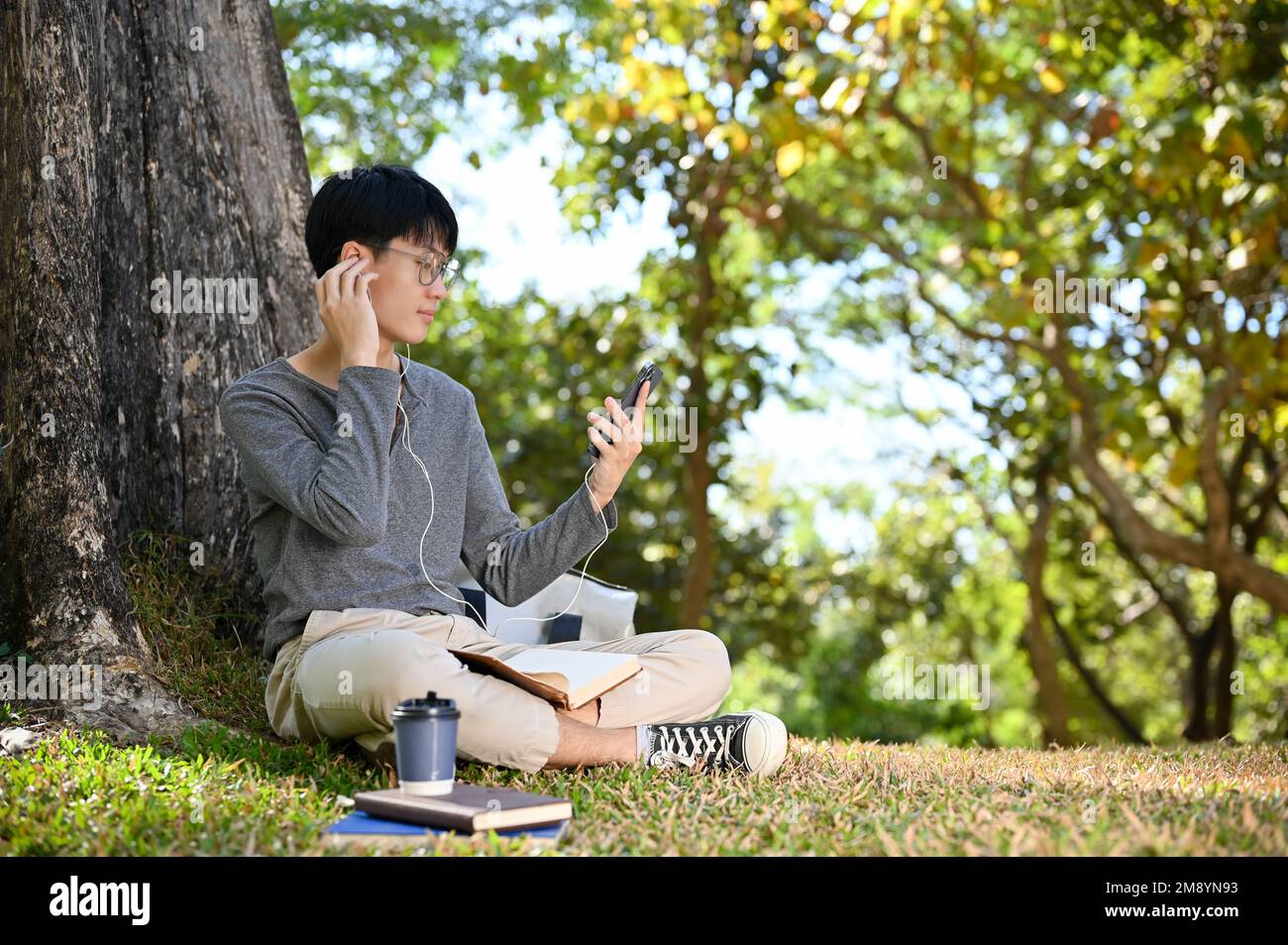 Happy and relaxed young Asian male college student listening to music ...