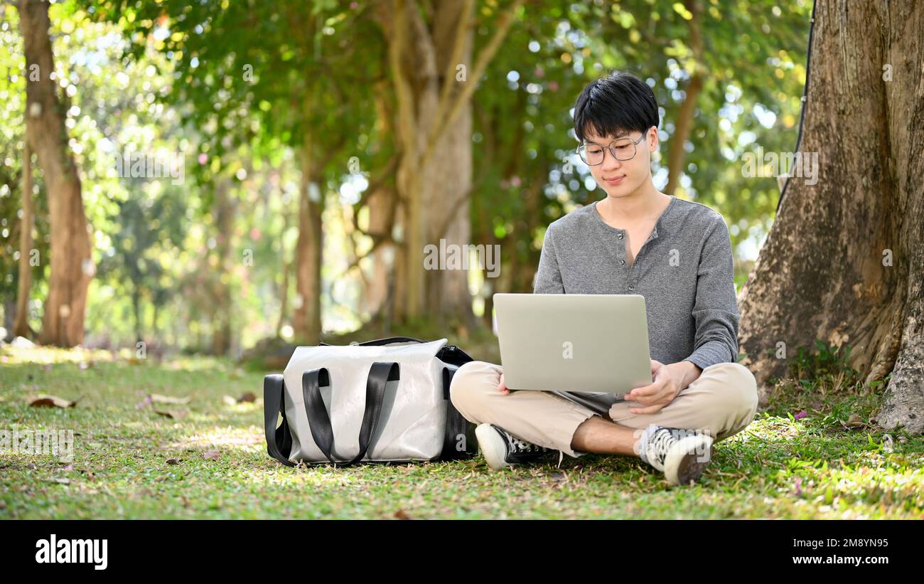 Smart and relaxed young Asian male college student using his portable ...