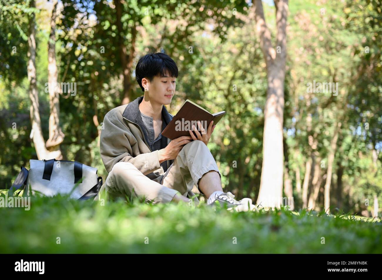 Chilling and focused young Asian male college student reading a book in ...