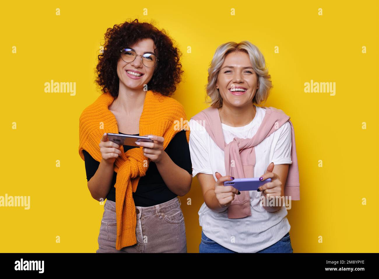 Two smiling young women gamer using smart mobile phone and playing ...