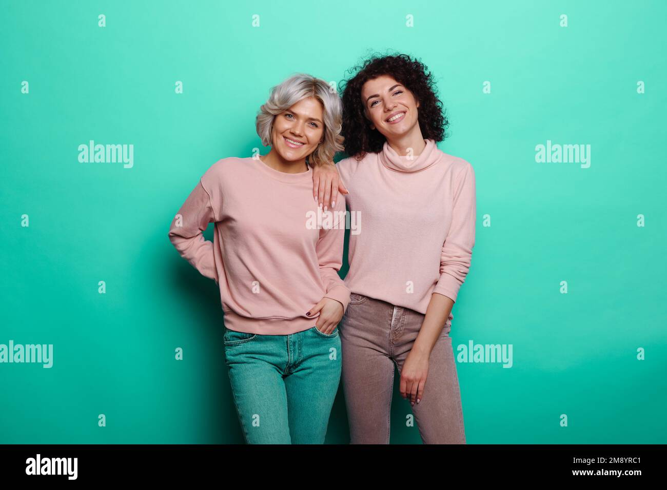 Two young beautiful smiling bwomen in casual clothes posing near blue ...