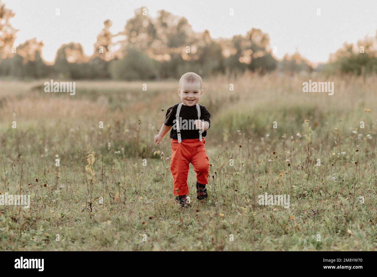 happy little baby boy running on summer grass in field. Added grain ...