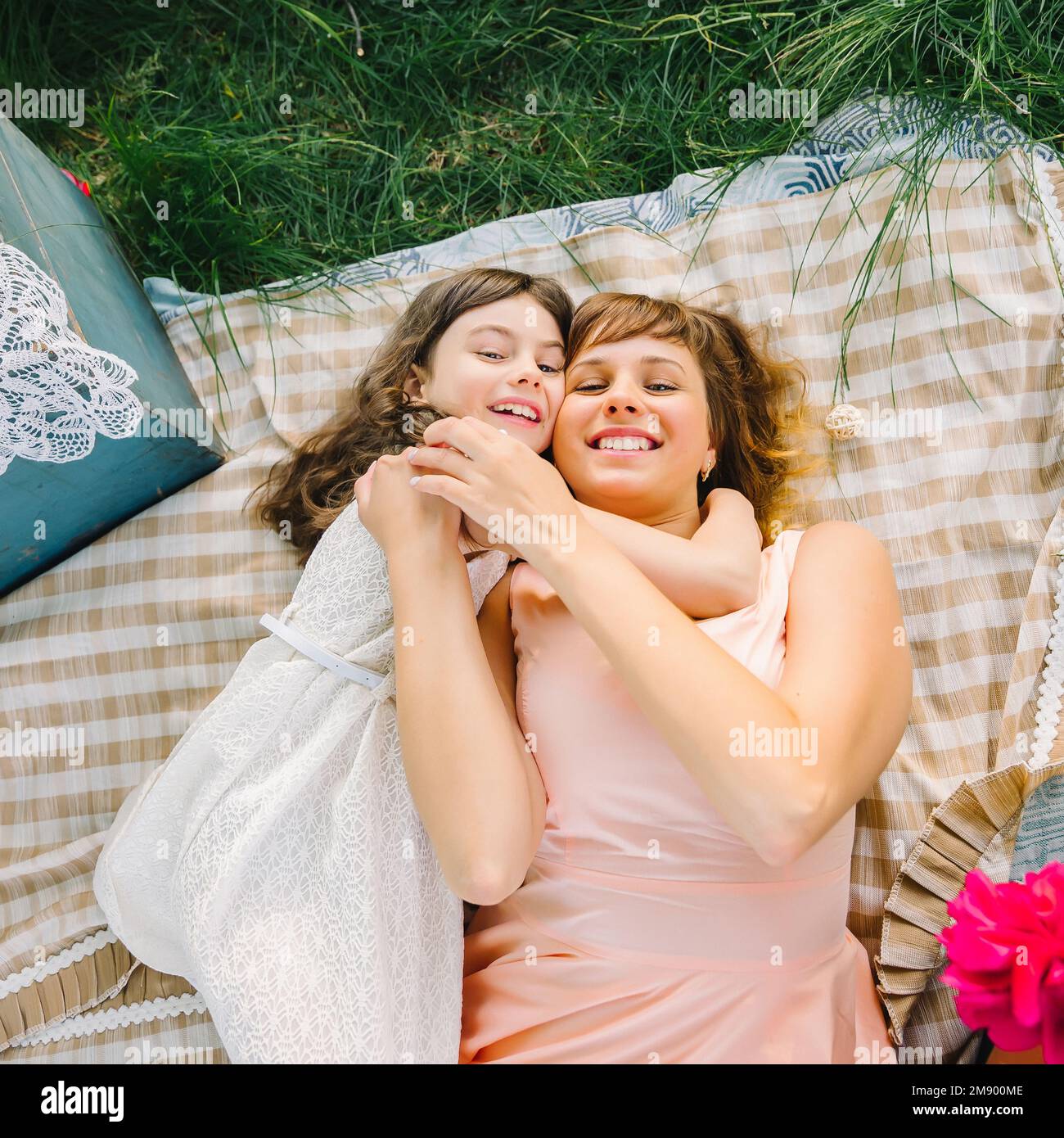 happy mother and daughter hugging lying down on a blanket in the summer ...