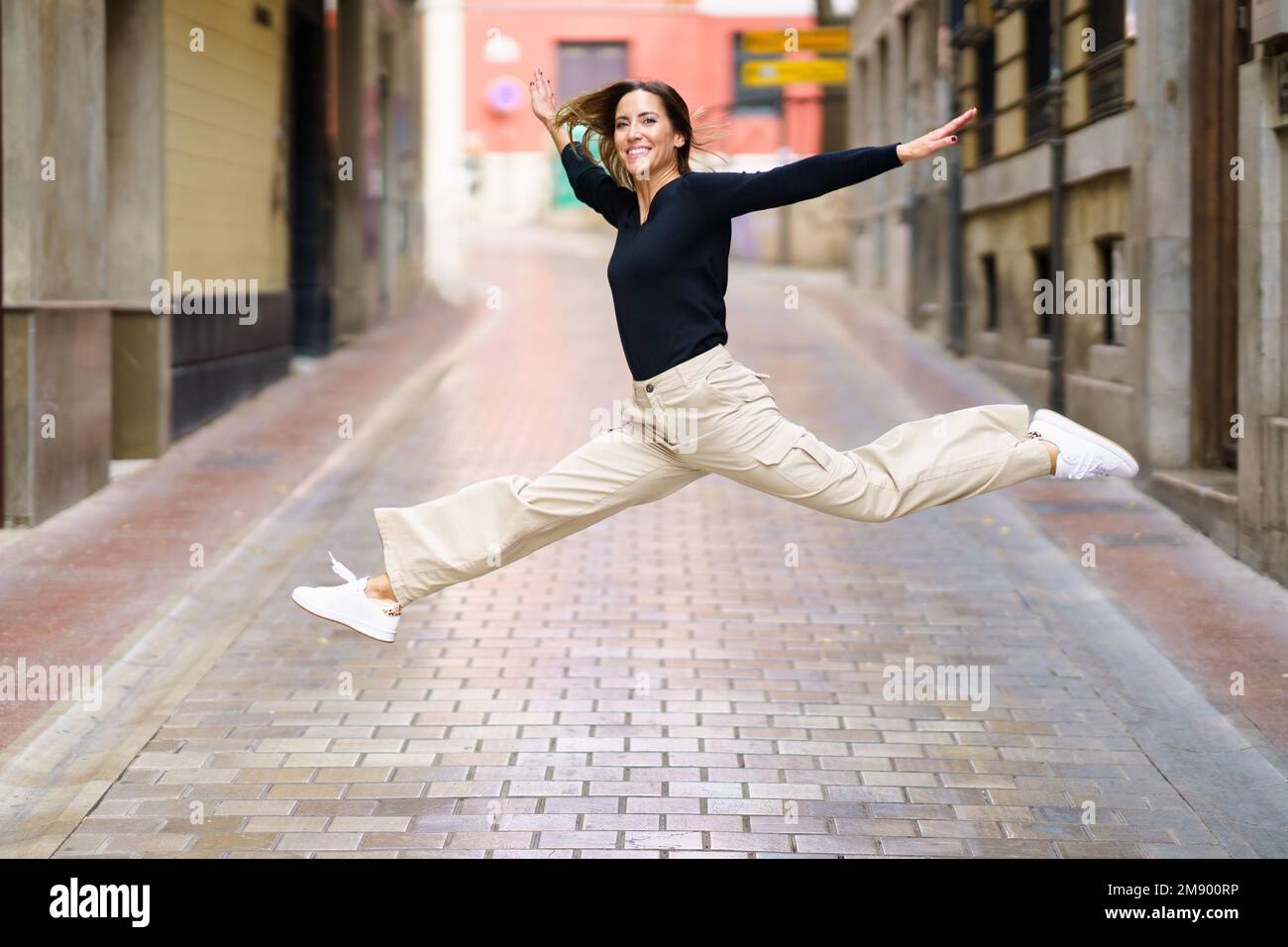 Excited young woman jumping on paved street and smiling Stock Photo - Alamy