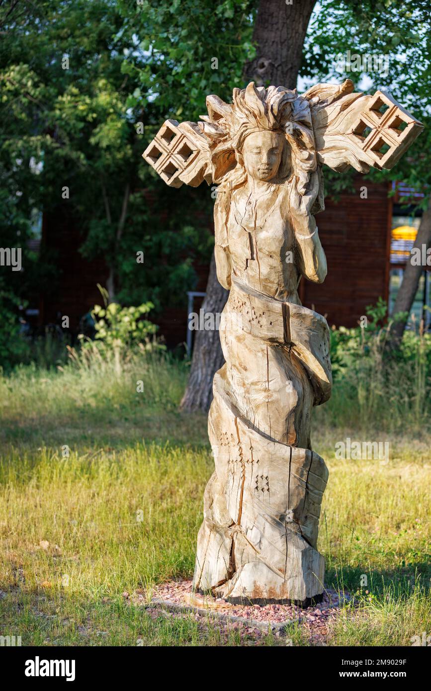 Wooden carved statue of a dancing Slavic girl in the sun on a blurred ...