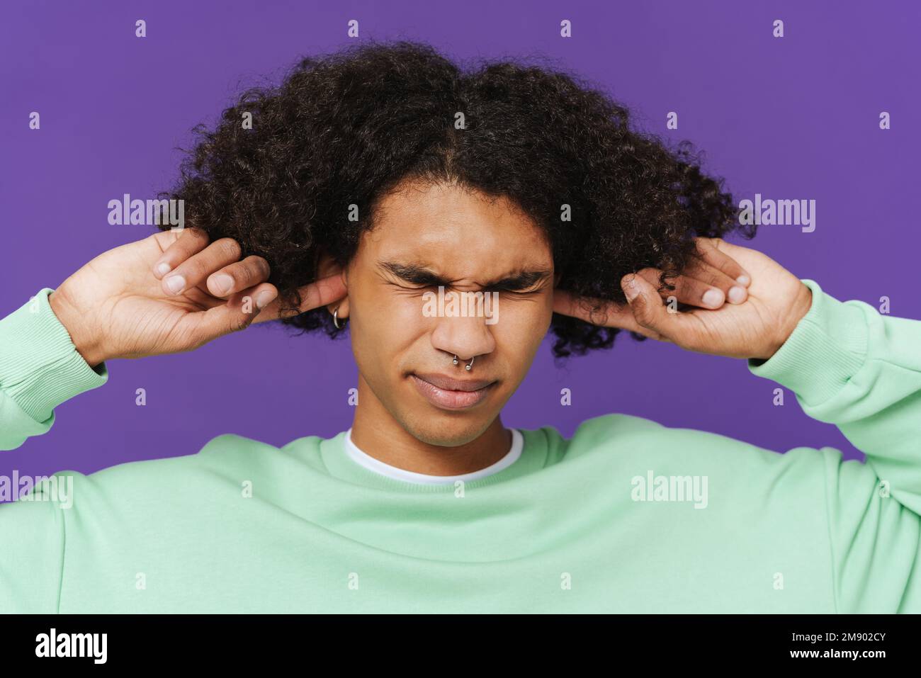 Young caribbean man with piercing plugging his ears isolated over ...