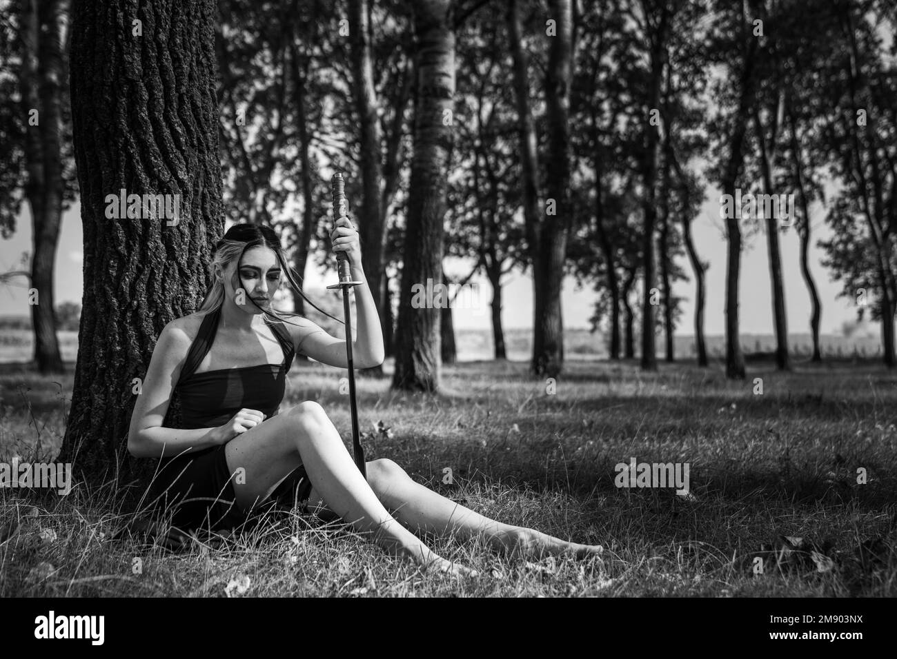 A grayscale of a young Caucasian girl holding a sword sitting under a ...