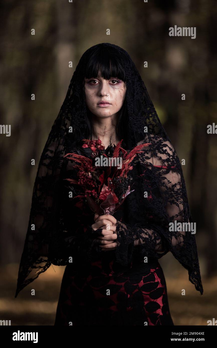 A vertical portrait of a scary corpse bride holding red flowers in the ...